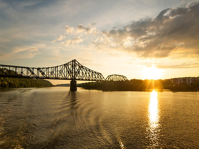 The bridge silhouetted against a golden sunset creates the kind of moment that makes you pull over, grab your phone, and still fail to capture its true magic.