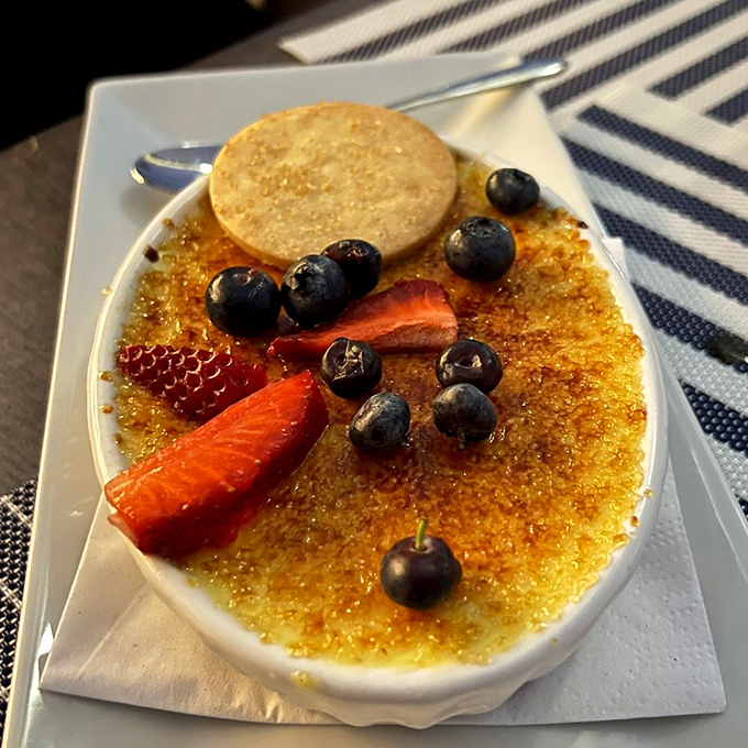 Cr&egrave;me br&ucirc;l&eacute;e with a perfectly shattered sugar ceiling, surrounded by berries that look like they're attending a very exclusive dessert gala.