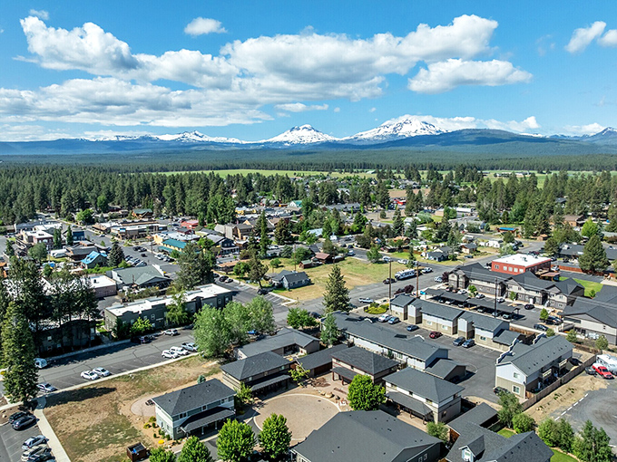 An aerial view revealing Sisters' perfect positioning: civilization comfortably nestled between mountain majesty and forest serenity, like nature's favorite middle child.