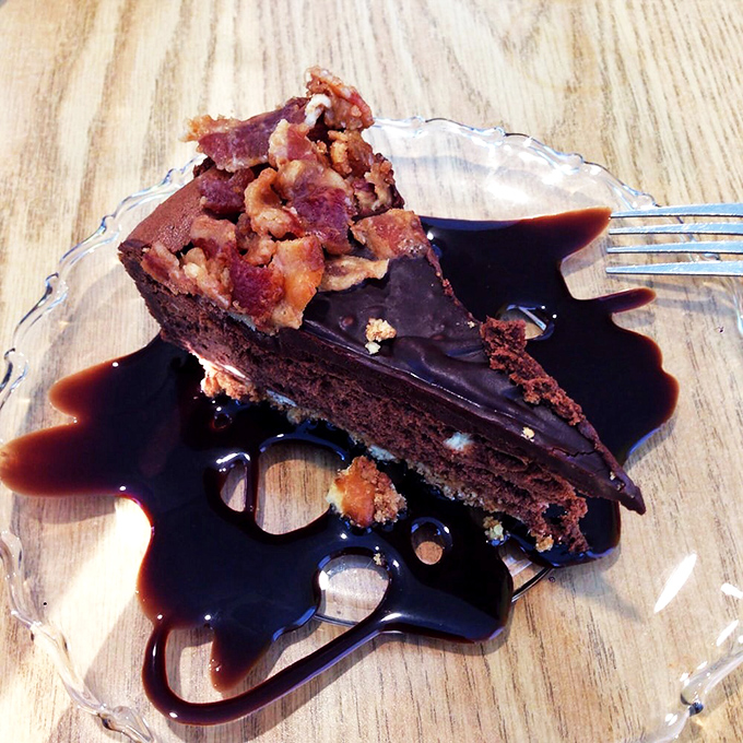 Chocolate cake draped in ganache with bacon crumbles on top – because sometimes dessert needs to dress up and show off a little.