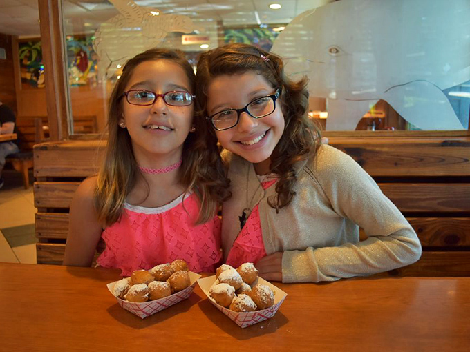 The image shows two young diners enjoying what appears to be the restaurant's famous corn fritters, their expressions capturing the simple joy of good food shared together.