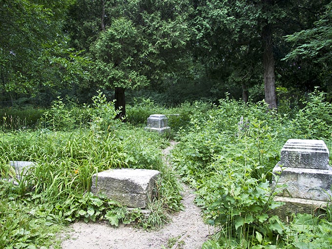 Summer greenery threatens to swallow these forgotten stones. Nature's persistence offers a poignant reminder that even our memorials require human attention to endure.