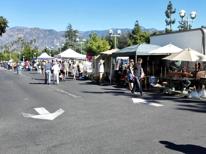 The thrill of the hunt! Shoppers stroll past vendor tents with mountains framing the scene&mdash;each step potentially leading to that perfect find.