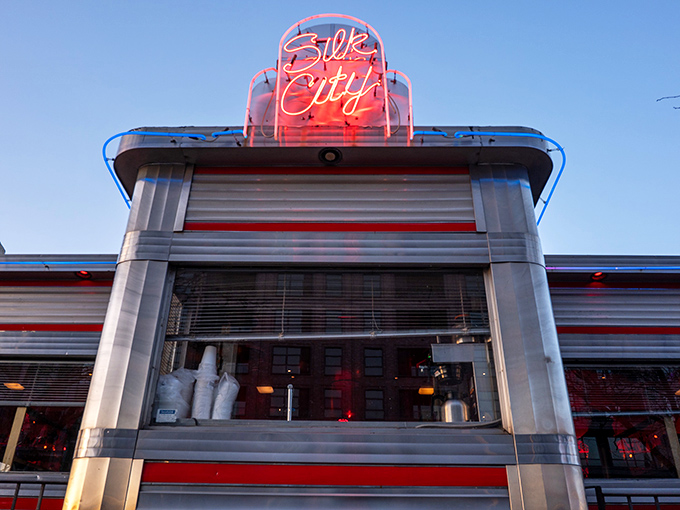 As dusk falls, the neon Silk City sign glows like a beacon for hungry souls seeking refuge from ordinary dining experiences.