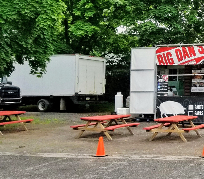 Red picnic tables under green trees—nature's perfect dining room for enjoying meat that's been kissed by fire and blessed by smoke.