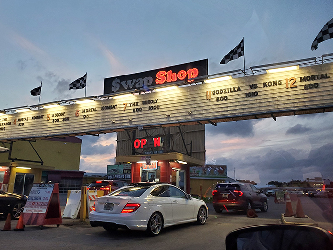 As dusk falls, the Swap Shop transforms into a drive-in theater. Movie titles illuminate the night, promising entertainment under the stars.