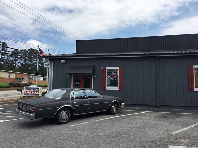 The gray exterior with red trim stands like a humble temple of smoke. Even that vintage car knows where to find the good stuff.