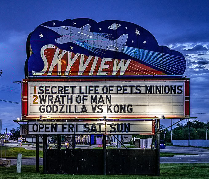The iconic Skyview sign glows against twilight skies, advertising monster battles and minion hijinks. Weekend plans, illuminated in neon glory.