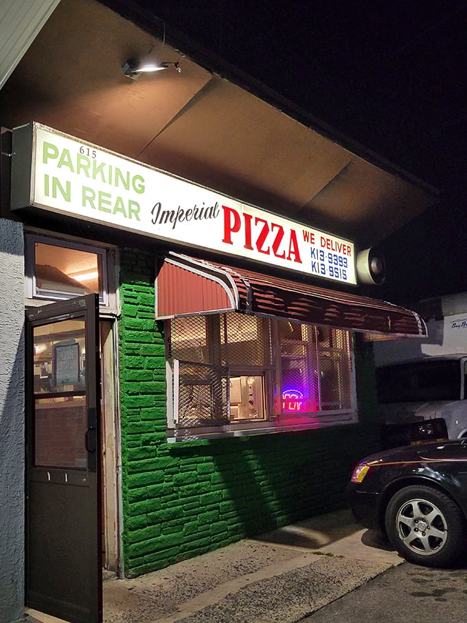 By night, the green-painted storefront glows with promise. That neon "OPEN" sign might as well say "Pizza Paradise Awaits" to those in the know.