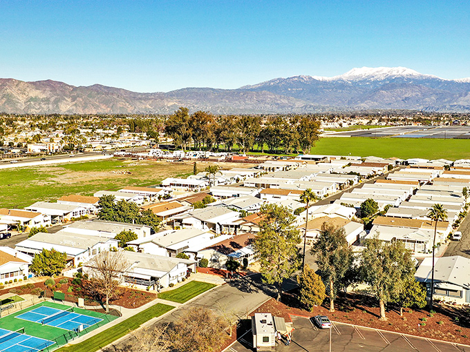 Aerial view of The Lakes at Hemet West, where retirement dreams meet mountain backdrops. Snow-capped peaks watch over neat rows of homes like nature's guardians.