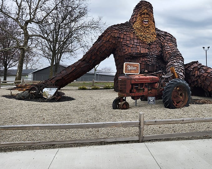 Standing tall beside vintage farm equipment, this carved cryptid proves that legends and agriculture make perfect neighbors.