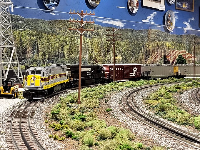 This yellow and black diesel locomotive leads a freight train through meticulously crafted mountain scenery that would make Bob Ross reach for his tiny brushes.