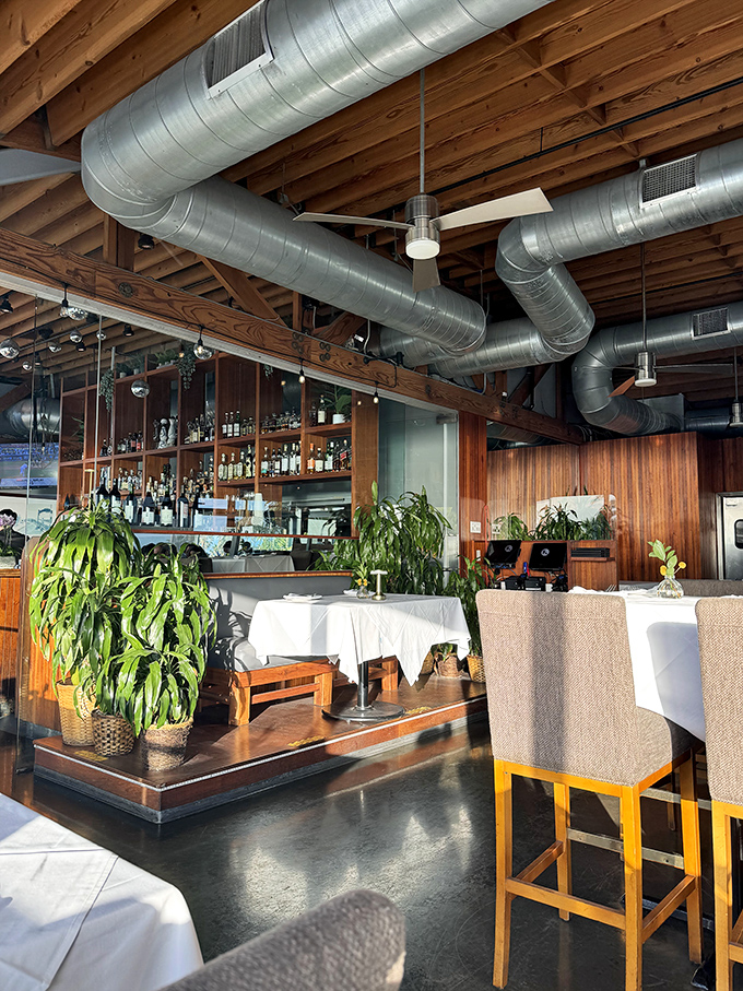 Industrial chic meets coastal comfort in this thoughtfully designed dining room where exposed beams frame ocean dreams perfectly.
