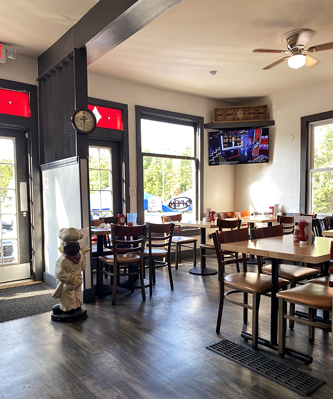 Inside, sunlight streams through large windows illuminating wooden tables where morning rituals unfold, while the chef statue stands guard over breakfast dreams.