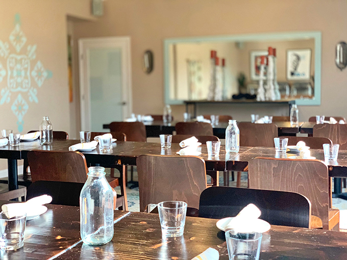Simple wooden tables await hungry diners, where water bottles stand ready for the inevitable "I need a moment" after that first bite of spice.