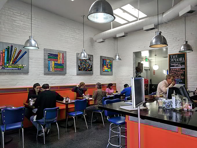 Inside, bright orange booths and blue chairs create a retro-modern collision course where art meets appetite in this vibrant dining space.