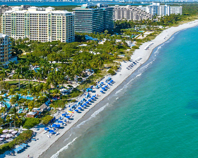 Resort life meets island tranquility along Key Biscayne's pristine shoreline, where blue umbrellas dot the sand like sapphires scattered by a generous hand.