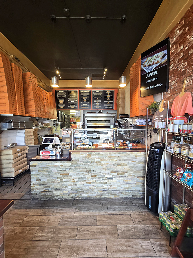 Inside awaits pizza nirvana with stacked boxes promising deliciousness. The stone counter says "serious business" while the menu board whispers "life-changing decisions ahead."