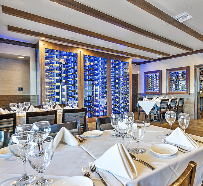 Wine walls that glow blue like the ocean depths frame immaculately set tables, creating an atmosphere that's both elegant and unmistakably coastal.
