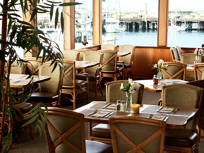 Floor-to-ceiling windows frame harbor views while comfortable seating whispers "stay awhile, the show's just beginning."