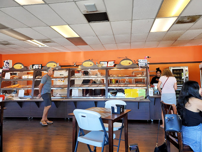 Inside, the vibrant orange walls and well-stocked display cases create a warm welcome that's as inviting as the aroma of fresh-baked bread.