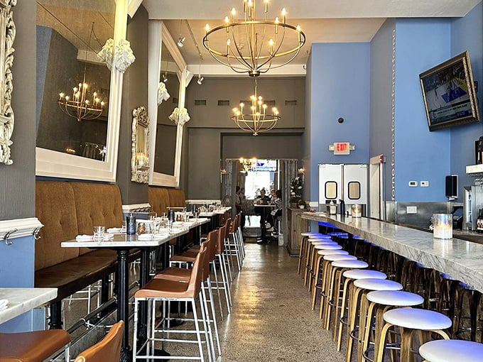 Elegant chandeliers illuminate the sleek marble bar, where blue walls and leather seating create an atmosphere that says "fancy enough for date night, comfortable enough for Tuesday."