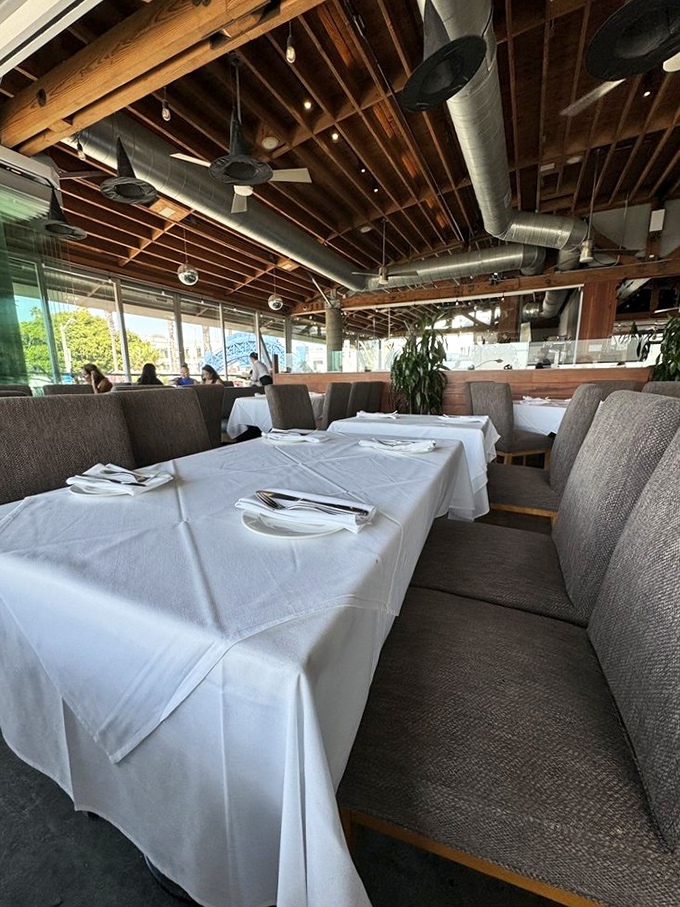 Exposed wooden beams meet crisp white tablecloths in this dining room where the industrial-chic ceiling doesn't dare compete with the ocean panorama just beyond those windows.
