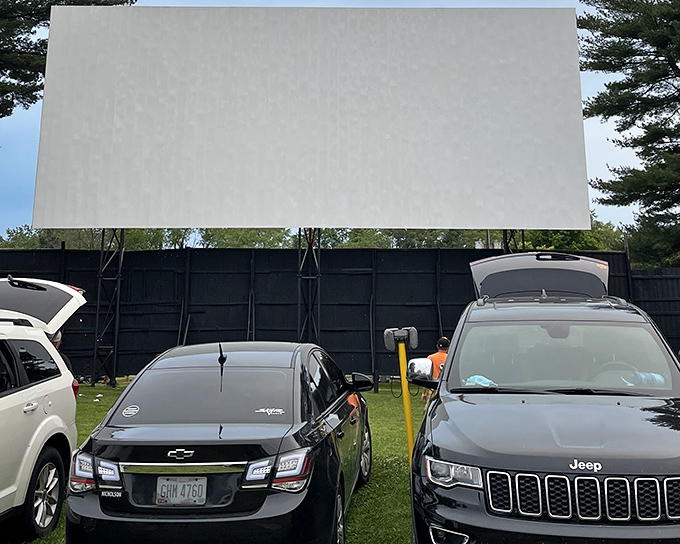 The massive white screen awaits dusk at Lynn Auto Theatre, standing tall against a backdrop of towering pines.