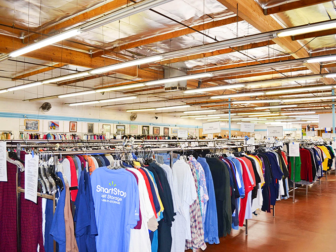 A rainbow of previously-loved garments awaits new adventures. The exposed wooden beams overhead watch as countless fashion stories begin their second chapters.