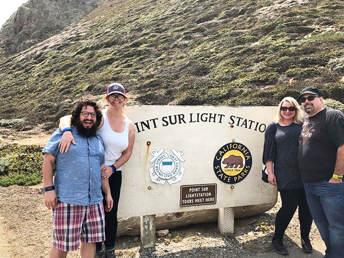 Visitors gather at the entrance sign, their expressions showing that mix of "we made it" and "wait, we still have to climb that?"