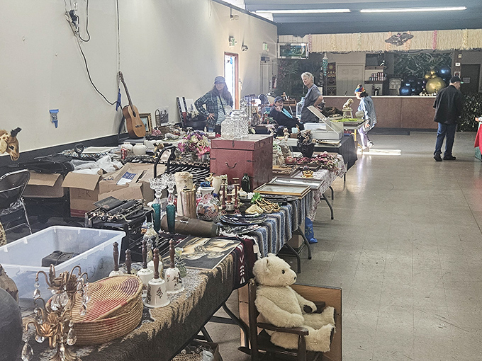 A teddy bear patiently waits for a new home amid vintage glassware and forgotten treasures. Every table holds potential magic.