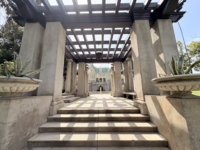 The pergola frames the mansion like nature's own viewfinder, creating an architectural runway that practically begs for a dramatic entrance.