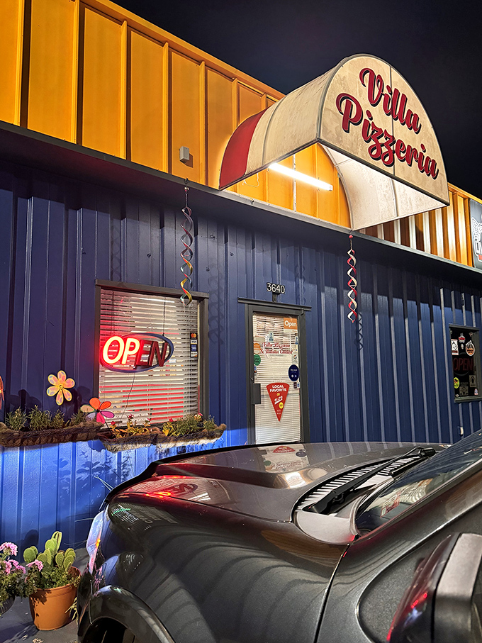 Night transforms this blue pizzeria into a glowing beacon of comfort. Villa's evening ambiance promises warm, cheesy delights.