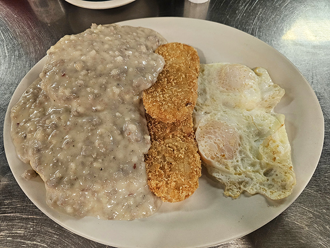 Behold the star attraction: biscuits drowning in creamy sausage gravy that could make your cardiologist weep and your taste buds sing hallelujah.