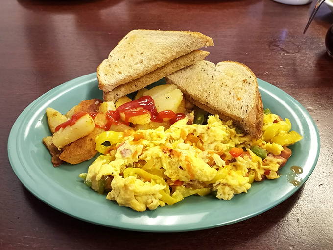Breakfast perfection on a turquoise plate: scrambled eggs bursting with color, home fries glistening with potential, and toast standing by for yolk-sopping duty.