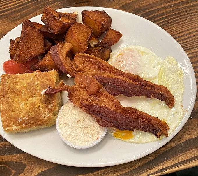 Breakfast perfection on a plate: crispy home fries, perfectly cooked eggs, thick-cut bacon, and a biscuit that would make your grandmother both proud and jealous.