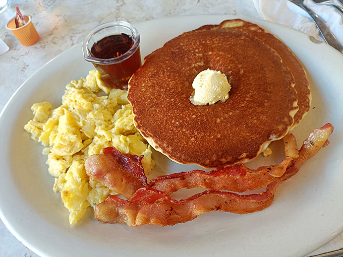The holy trinity of breakfast perfection: golden pancake, fluffy scrambled eggs, and bacon that's achieved that mythical balance between crisp and chewy.