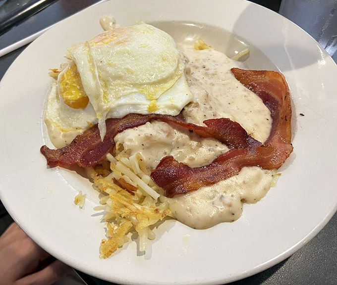 Breakfast architecture at its finest! Layers of hash browns, bacon, and gravy crowned with sunny-side-up eggs&mdash;a morning masterpiece that demands respect.