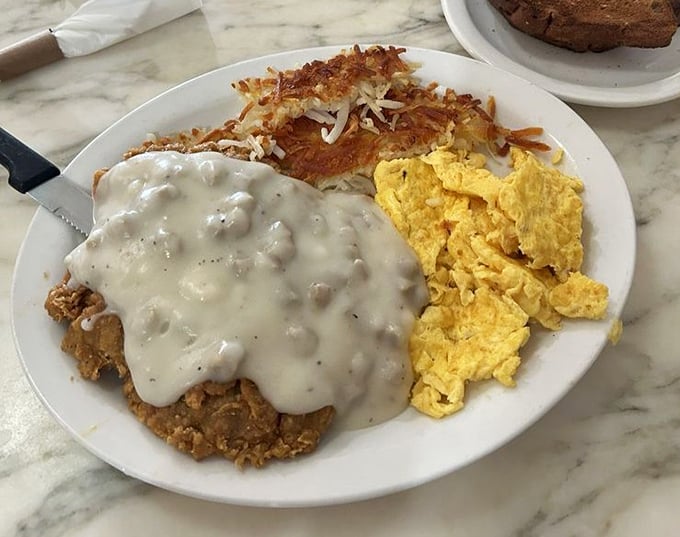 Country-fried steak swimming in peppery gravy alongside golden hash browns and fluffy scrambled eggs—the breakfast trinity that launched a thousand food dreams.