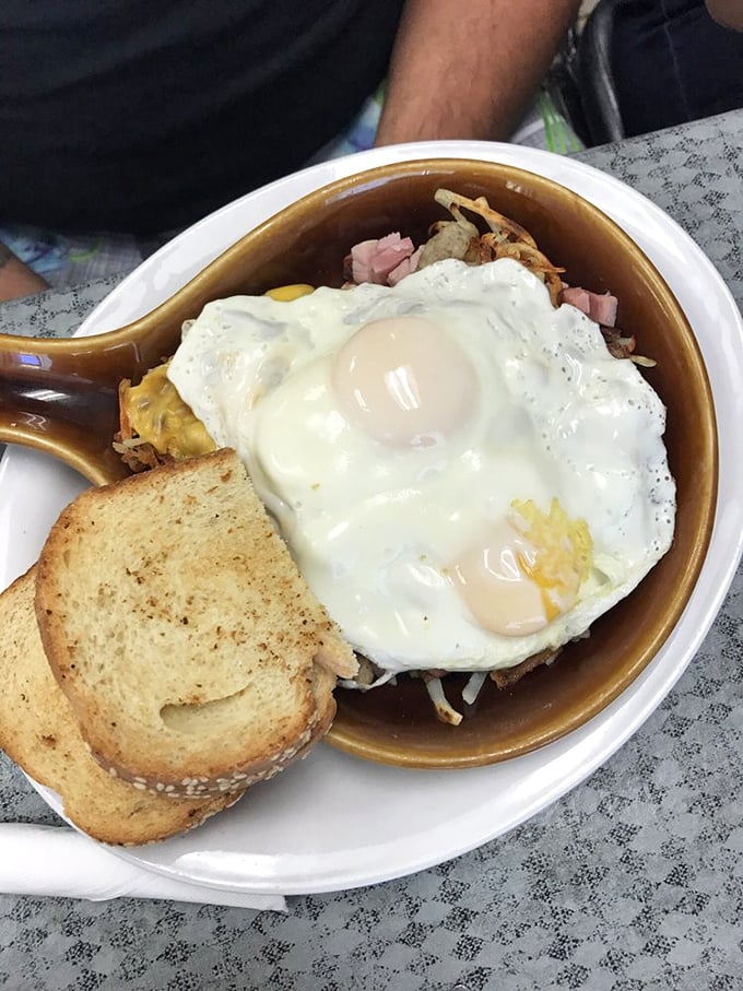 Breakfast perfection in a skillet &ndash; sunny eggs crowning a kingdom of potatoes, ham, and cheese. The toast stands ready for yolk-dipping duty.