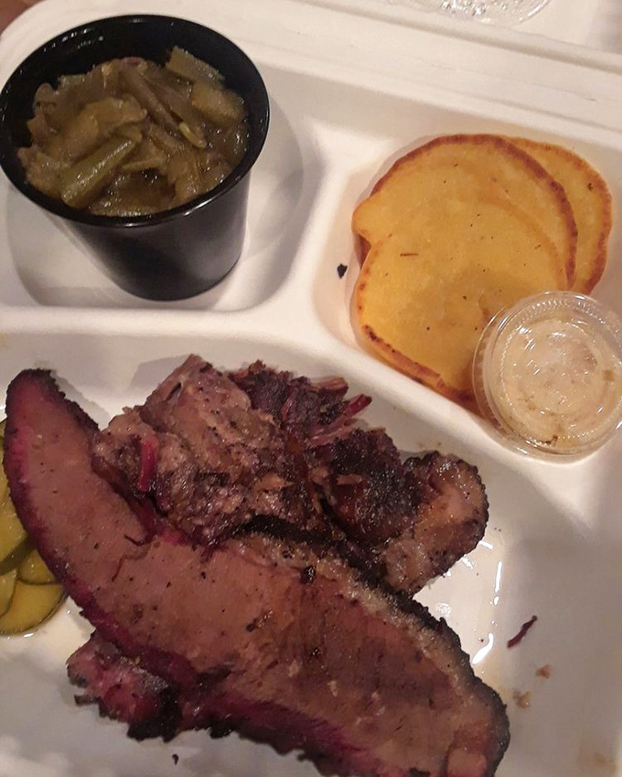 Behold the holy trinity of barbecue perfection: brisket with that coveted pink smoke ring, collard greens, and golden hoe cakes waiting for their moment.