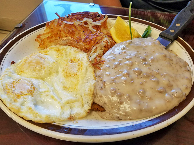 Country gravy cascading over golden-fried goodness alongside sunny eggs and crispy potatoes. Comfort food that hugs your soul before noon.