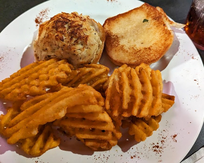 Comfort on a plate: a golden-brown crab cake, seasoned potato, and those addictive waffle fries. Carb heaven with coastal flair.