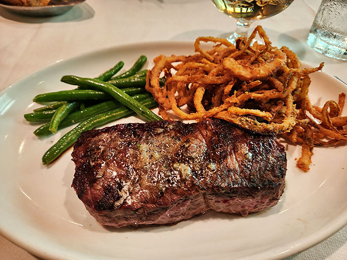 Behold the Delmonico in its natural habitat &ndash; perfectly seared, accompanied by crispy onion strings and green beans that actually taste like vegetables should.