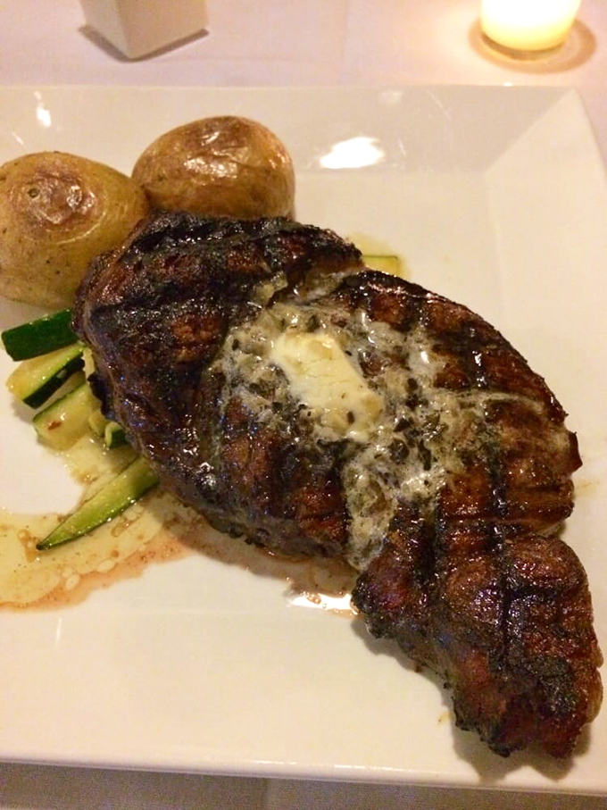 This perfectly seared ribeye doesn't just sit on the plate—it commands attention with a crown of herb butter slowly melting into meaty perfection.