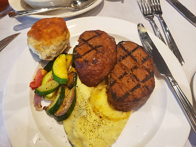 Two perfectly seared filet medallions rest atop whipped potatoes like meaty royalty, accompanied by seasonal vegetables and a biscuit fit for royalty.