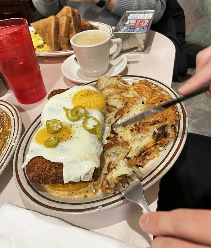 Breakfast nirvana achieved: crispy scrapple crowned with sunny-side eggs and jalapeños, alongside hash browns that crackle with each forkful.