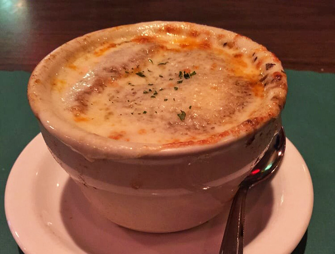 The legendary French onion soup arrives like a geological wonder—a molten cheese cap covering a steaming crater of caramelized onion bliss.