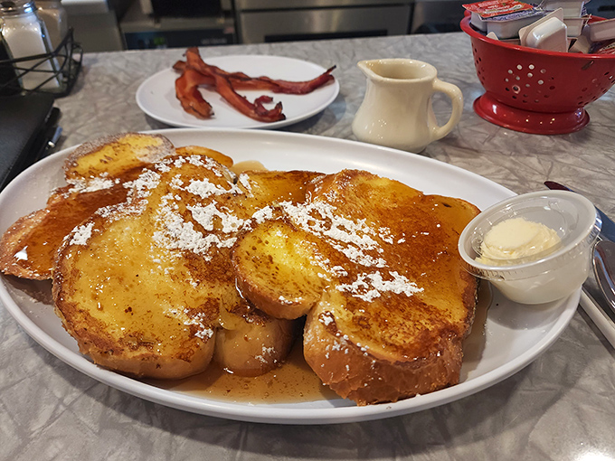 French toast nirvana! Golden-brown perfection dusted with powdered sugar, ready for its maple syrup baptism. Bacon on standby for the sweet-savory dance.
