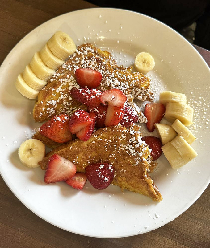 French toast that doesn't just arrive&mdash;it makes an entrance. Crowned with fresh strawberries and bananas, it's breakfast royalty dusted with powdered sugar confetti.